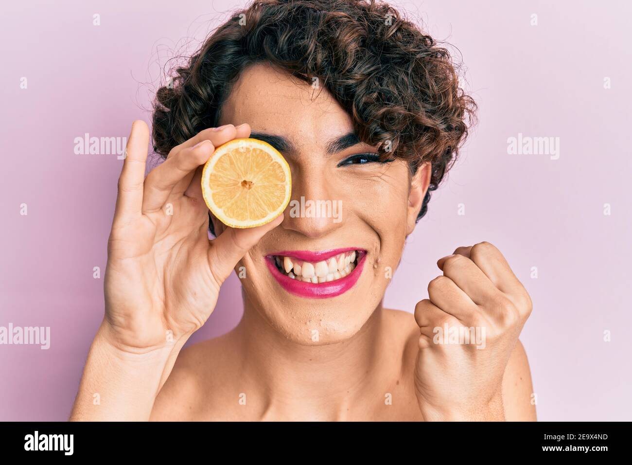Young man wearing woman make up holding lemon screaming proud ...