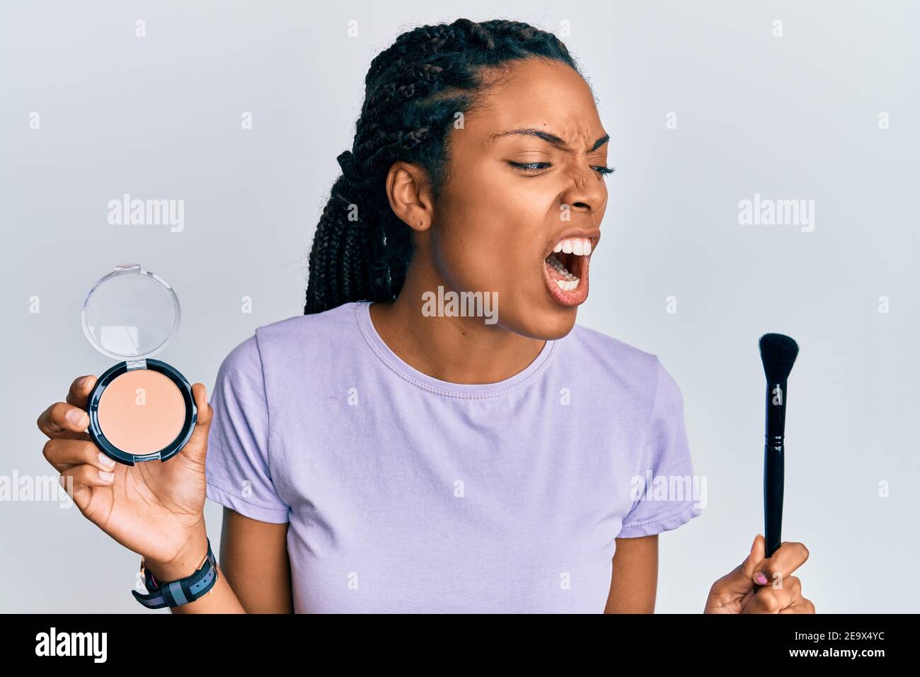 African american woman holding makeup brush and blush angry and mad ...