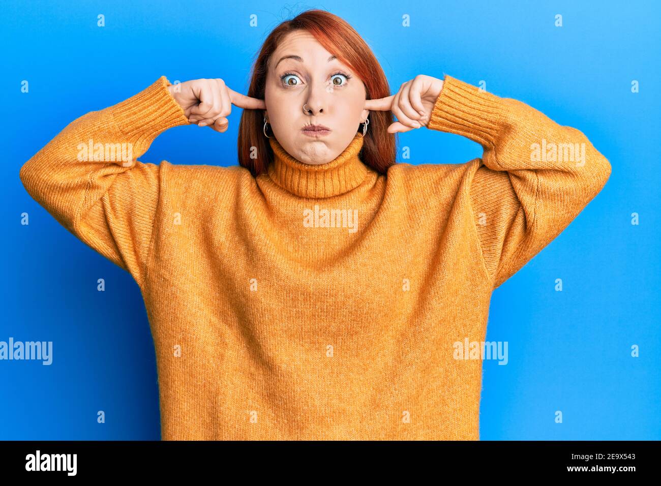 Beautiful redhead woman putting fingers on ears ignoring noise puffing ...