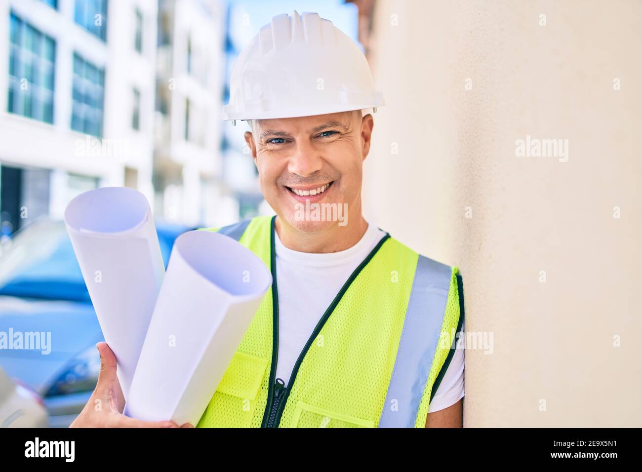 Middle age architect man holding blueprints leaning on the wall at the ...