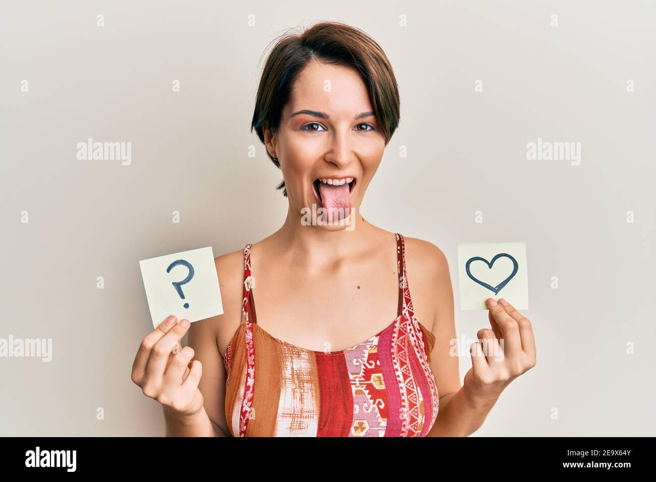 Young brunette woman with short hair holding heart and question mark ...