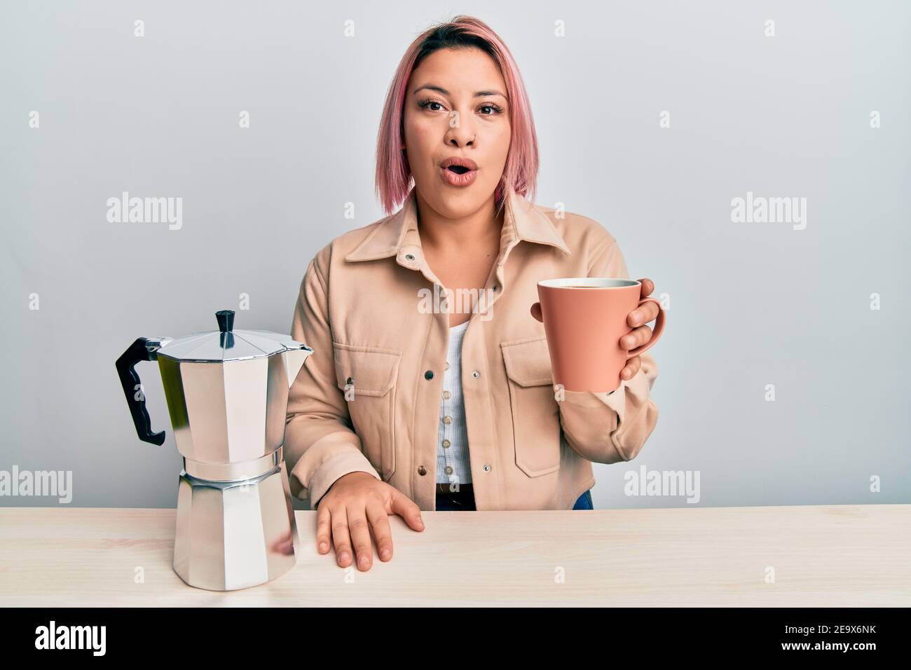 Hispanic woman with pink hair drinking a cup of italian coffee scared ...