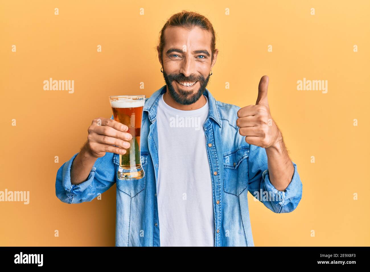 Attractive man with long hair and beard drinking a pint of beer smiling ...