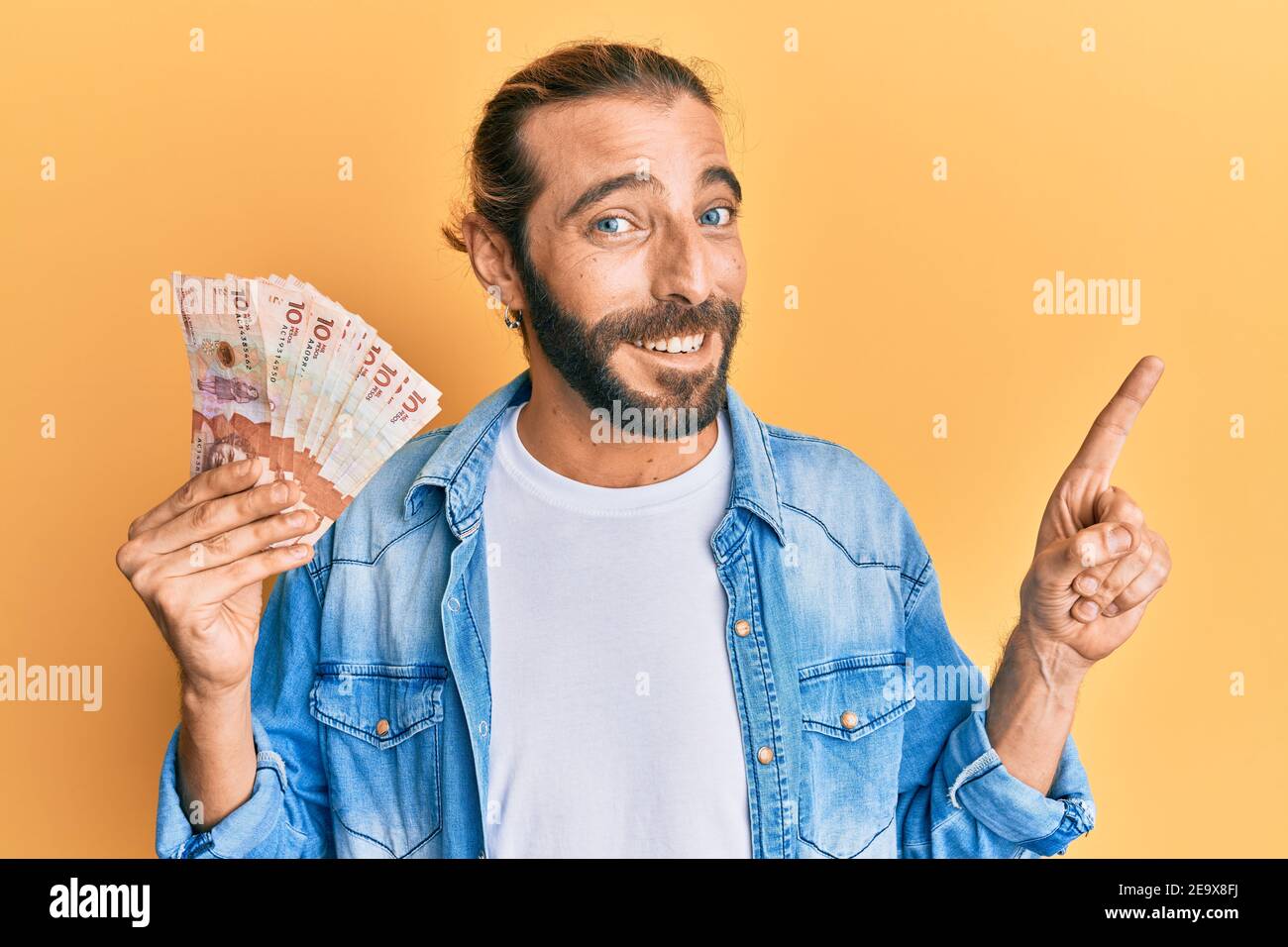 Attractive man with long hair and beard holding 10 colombian pesos ...