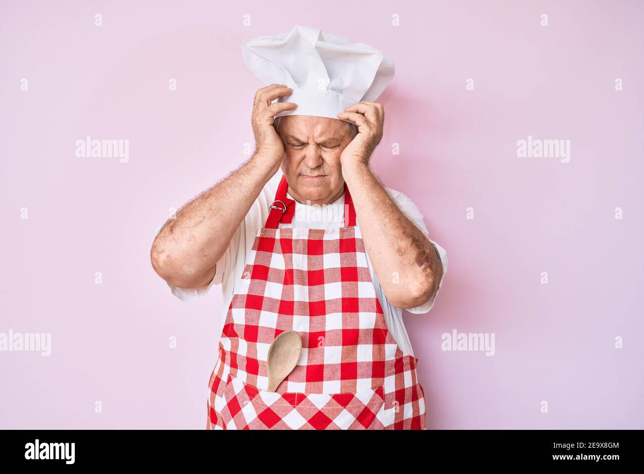 Senior grey-haired man wearing professional baker apron suffering from ...