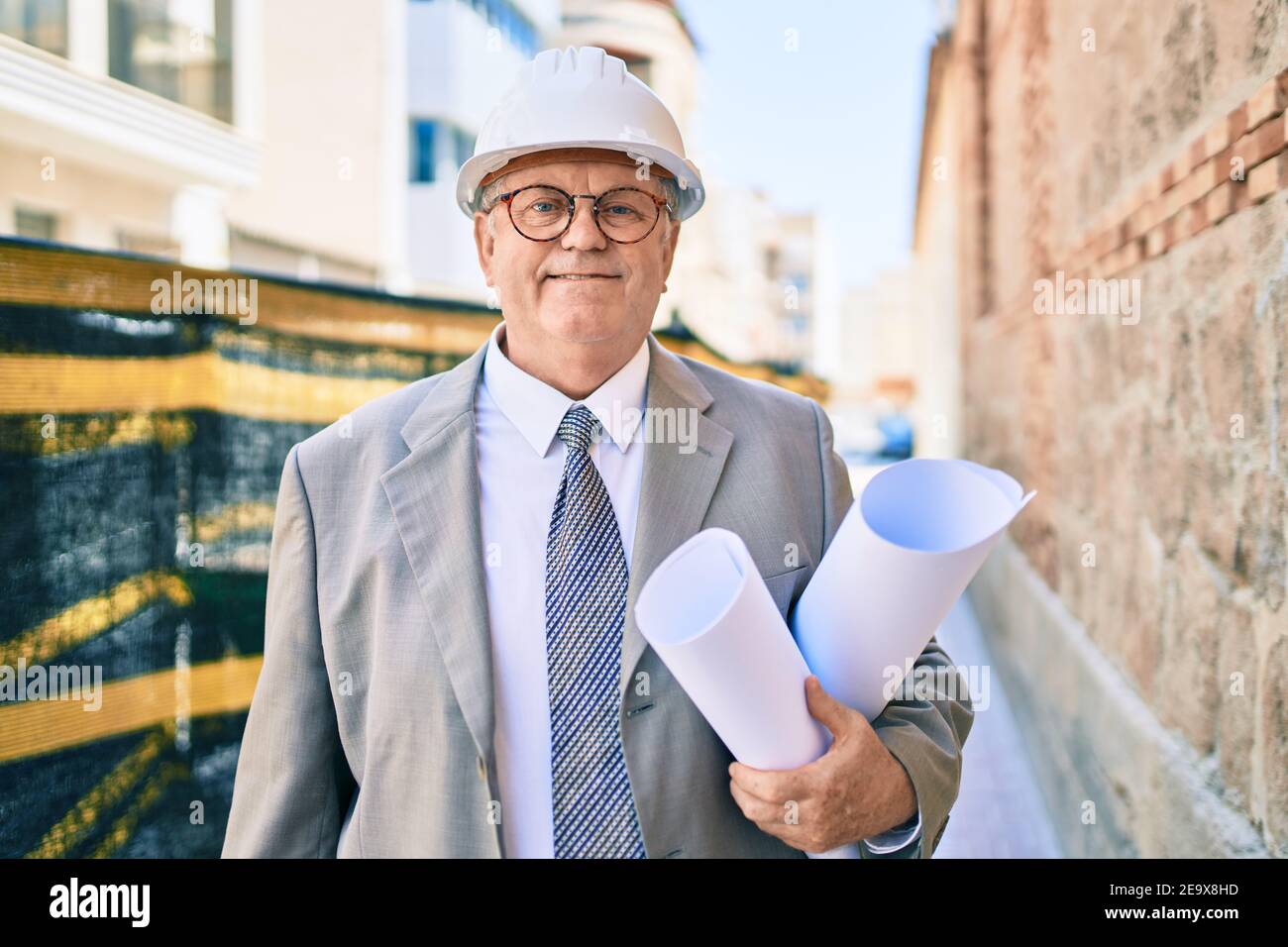 Senior grey-haired architect man holding blueprints walking at street ...