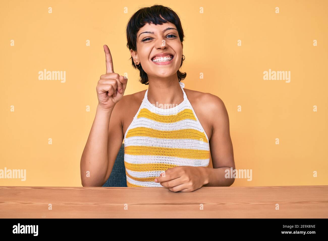 Beautiful brunettte woman sitting on the table over yellow background ...