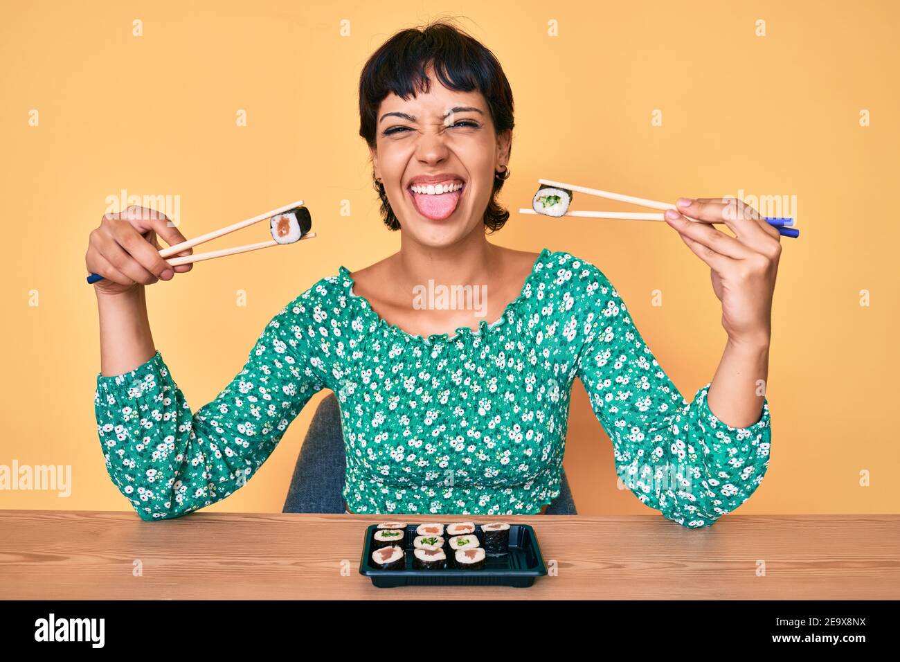 Beautiful brunettte woman eating sushi sitting on the table sticking ...