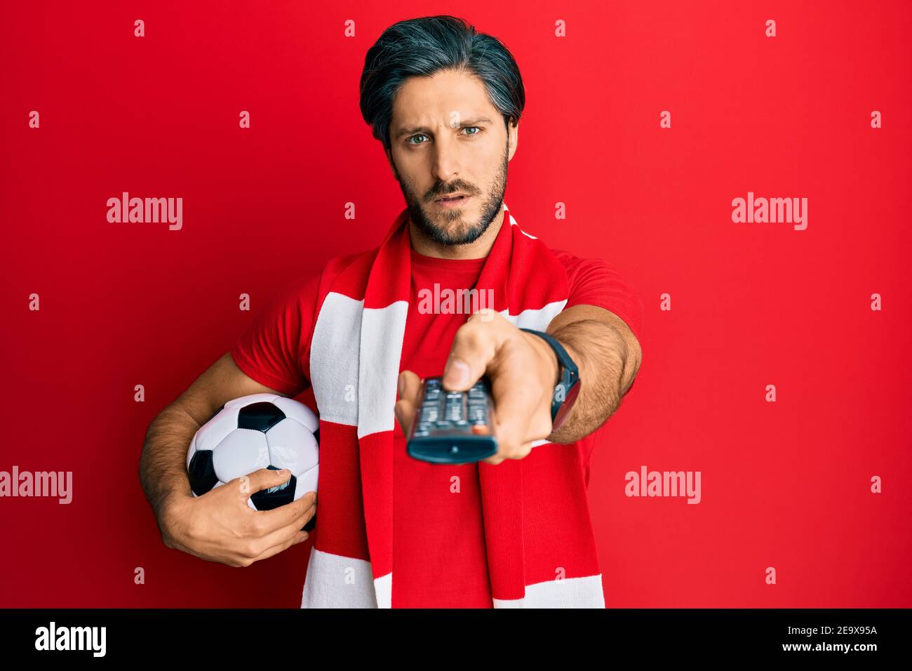 Young hispanic man football hooligan holding ball using tv control ...