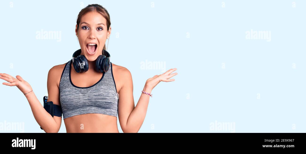 Young beautiful hispanic woman wearing gym clothes and using headphones ...