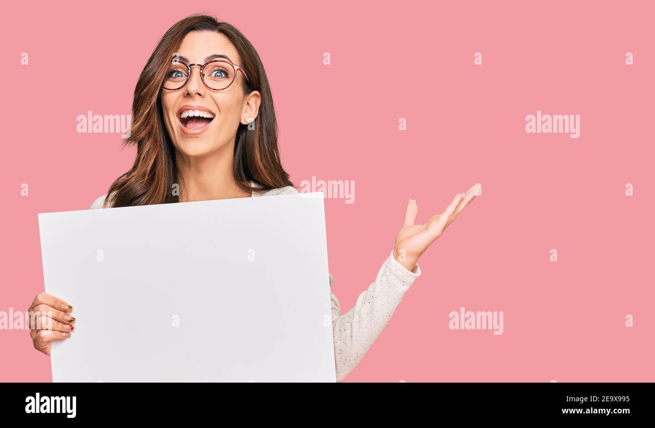 Young brunette woman holding blank empty banner celebrating victory ...