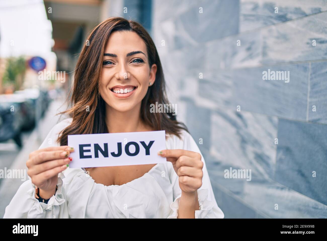Young hispanic woman smiling happy holding enjoy word paper standing at ...