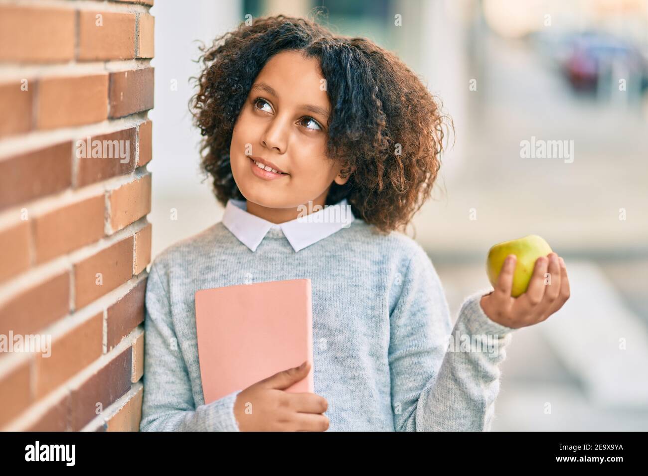 Adorable hispanic student child girl smiling happy holding green apple ...