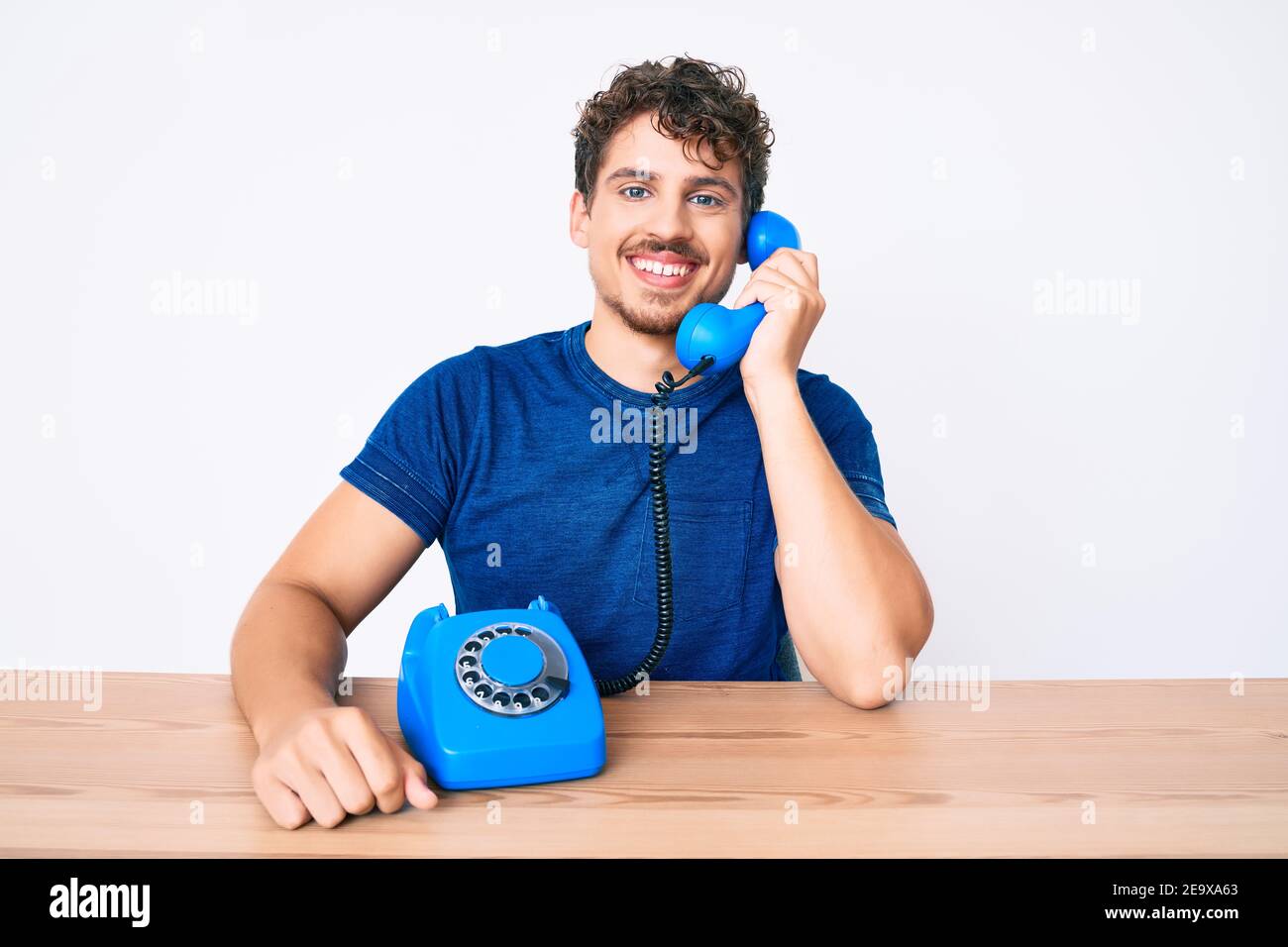 Young caucasian man with curly hair using vintage telephone sitting on ...