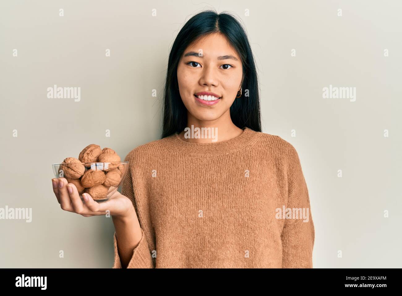 Young chinese woman holding bowl with walnuts looking positive and ...