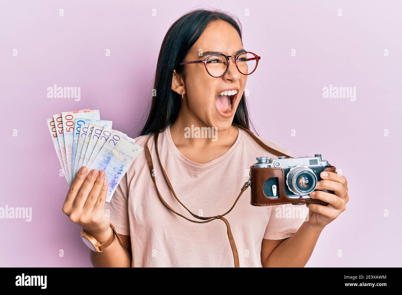 Young asian woman holding vintage camera and swedish krona angry and ...