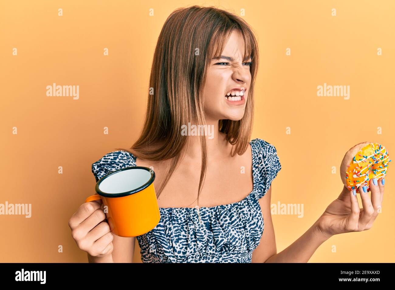 Teenager caucasian girl eating doughnut and drinking coffee angry and ...
