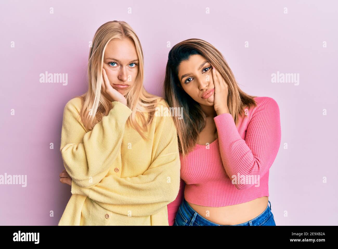 Two friends standing together over pink background thinking looking ...