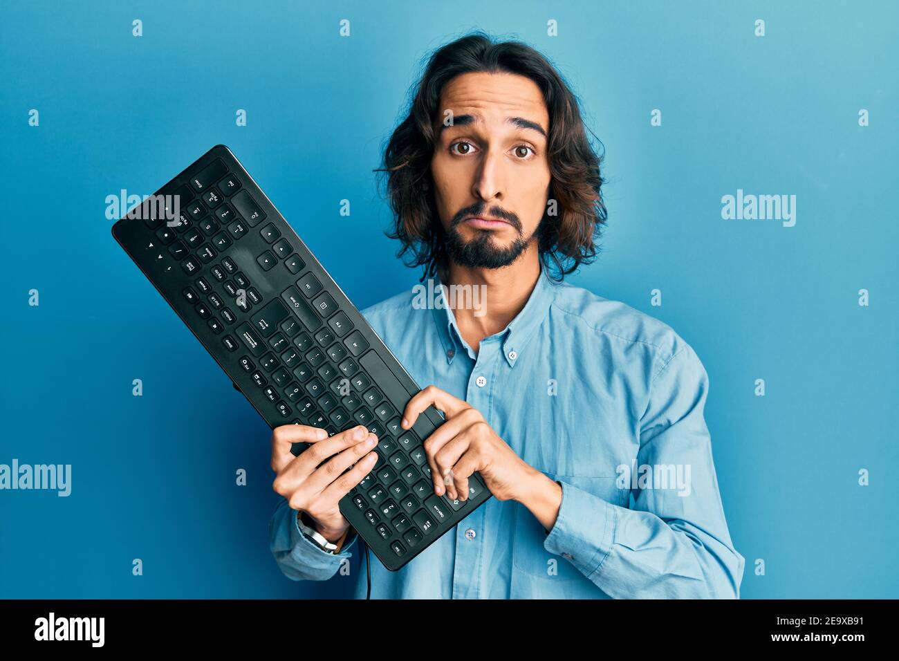 Young hispanic man holding keyboard depressed and worry for distress ...