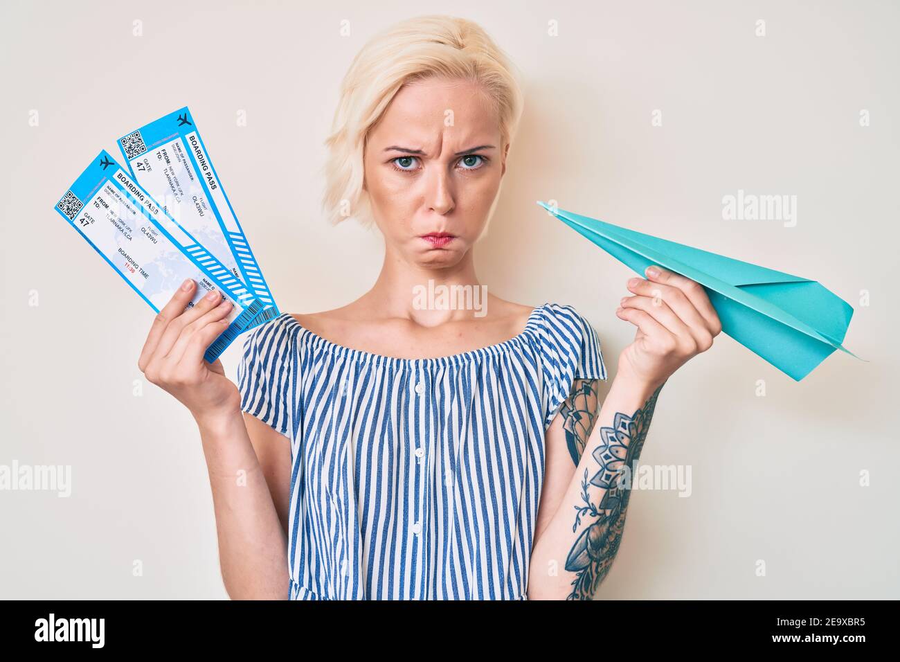 Young blonde woman with tattoo holding paper airplane and boarding pass ...