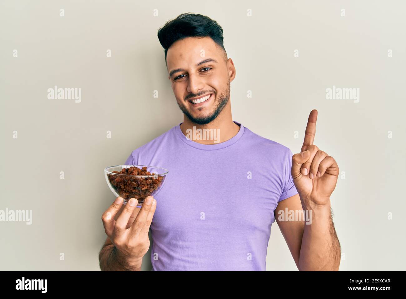 Young arab man holding raisins bowl smiling with an idea or question ...