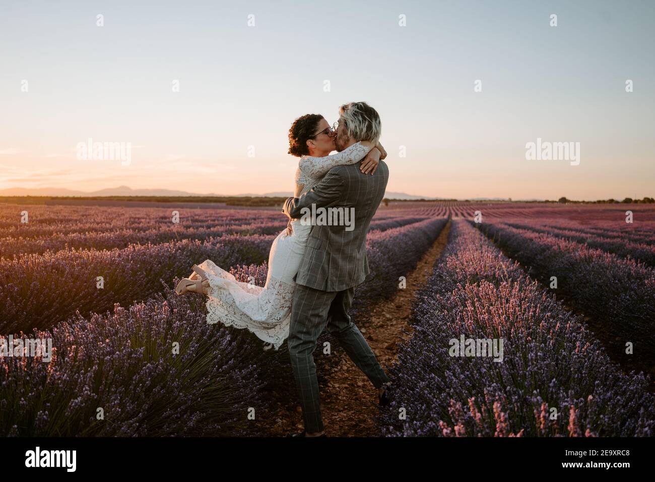Side view of groom lifting bride while standing in lavender field on ...
