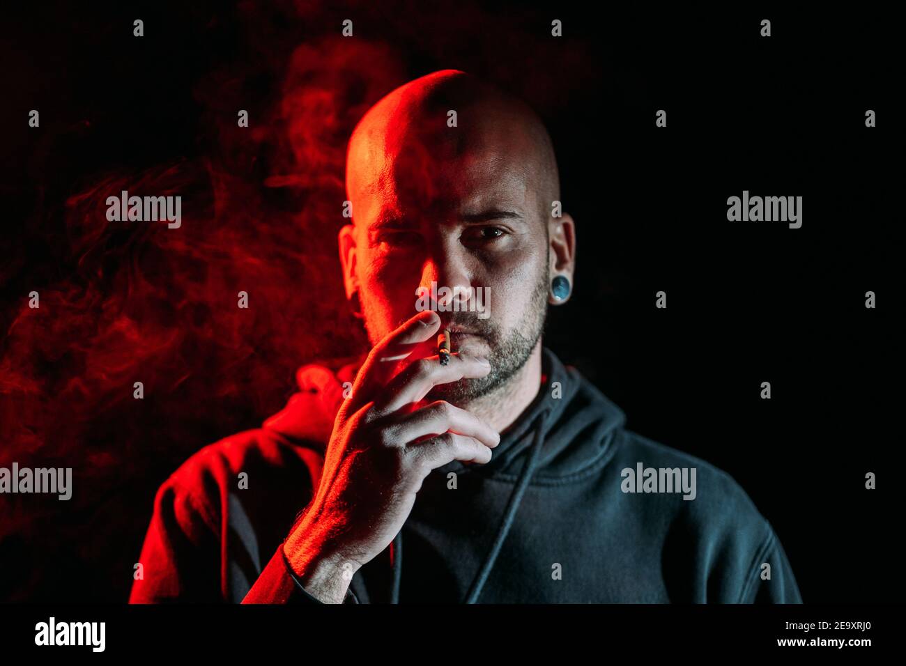 Serious male rocker smoking cigarette and looking at camera on black ...