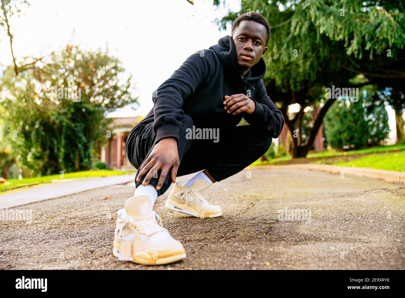 Low angle of young ethnic male in stylish apparel squatting on pathway ...