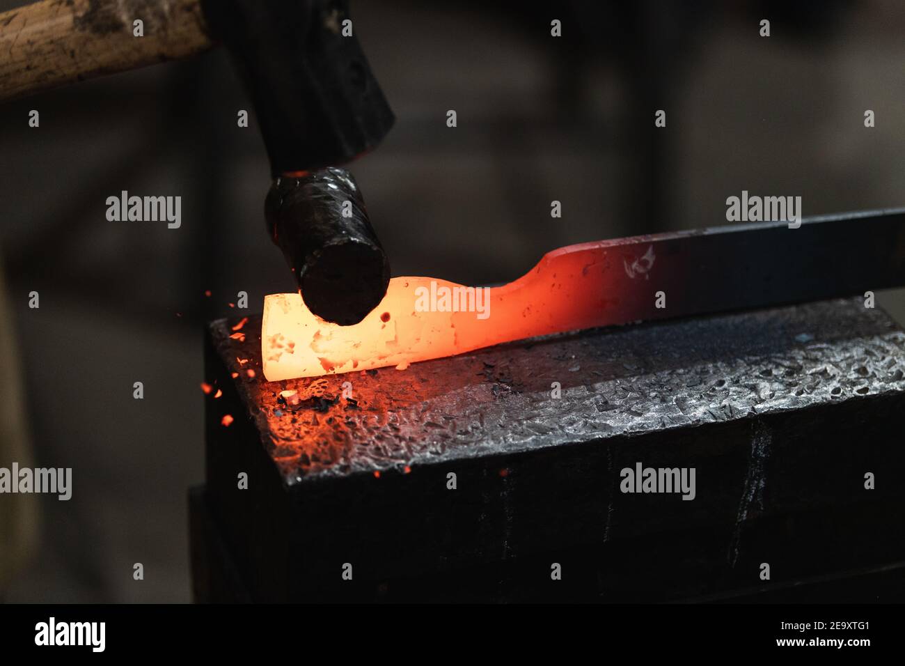 Unrecognizable craftsman hammering hot iron piece at anvil during ...