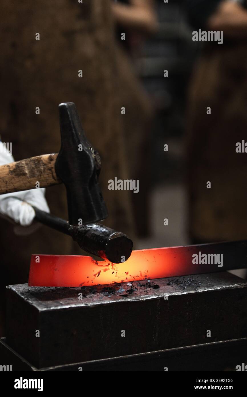 Unrecognizable craftsman hammering hot iron piece at anvil during ...