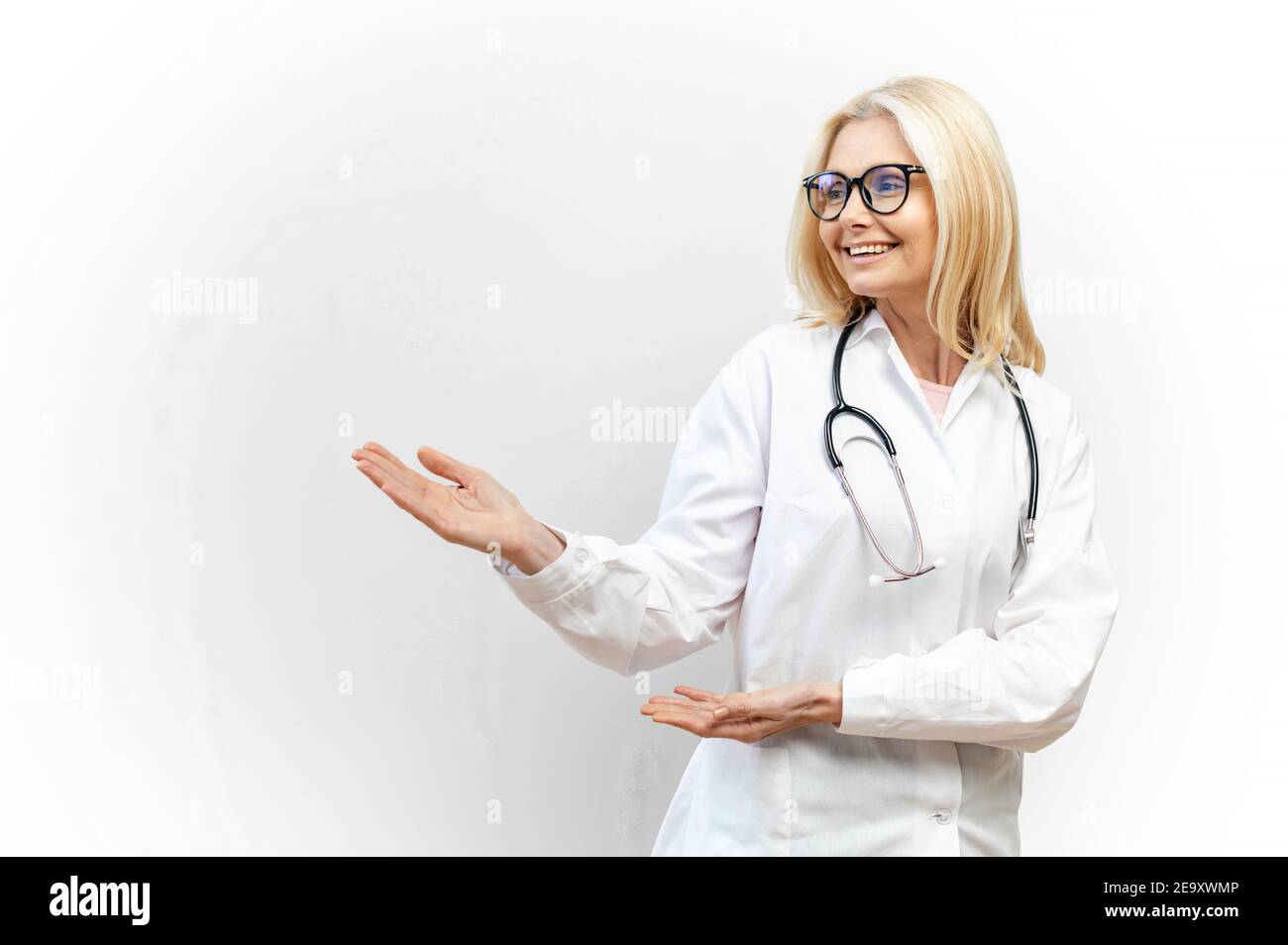 Cheerful and peppy female doctor points with hands on the empty space ...