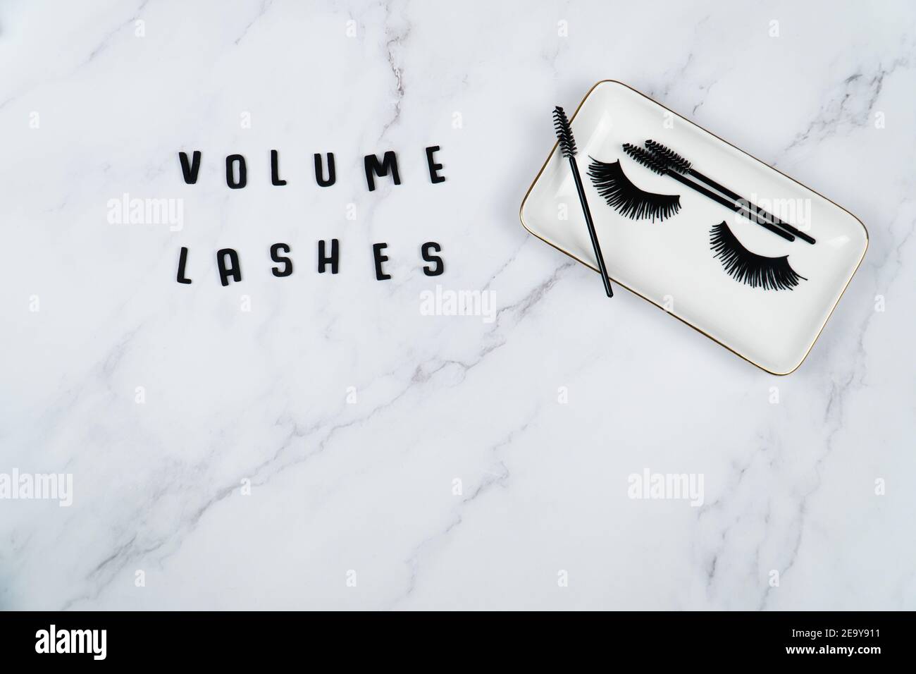 A beauty concept background with the words Volume Lashes in black with ...