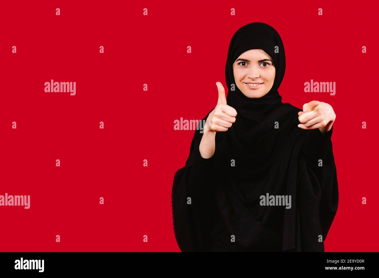 Smiling young arabian muslim woman in hijab black clothes pointing ...