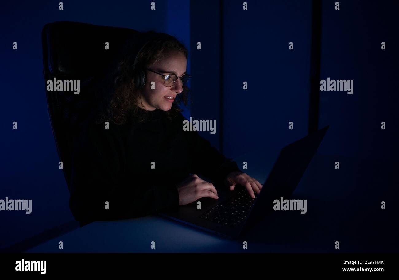 Gamer woman playing computer at night with wireless headphones. There ...