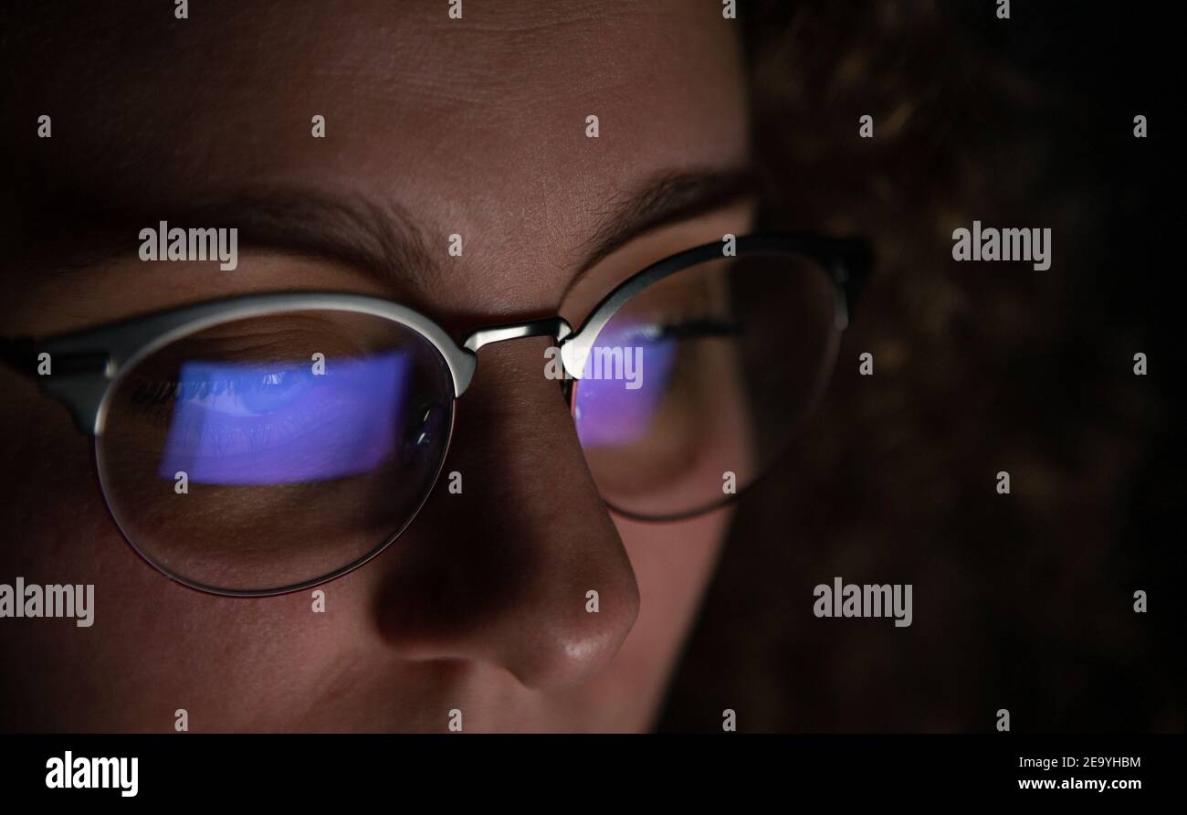 Computer screen reflected in the glasses of a woman who is working at ...