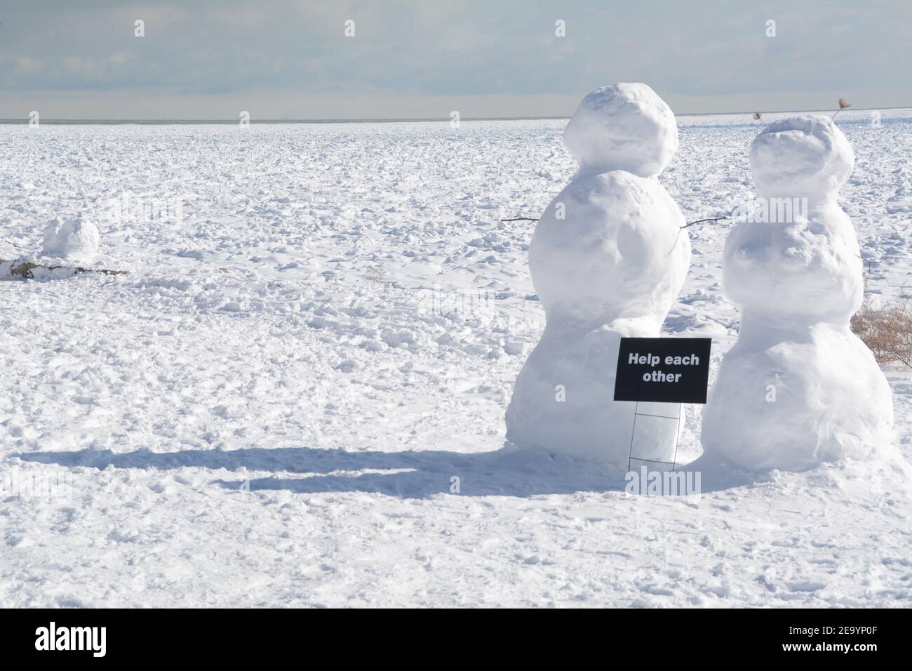 Two snowmen with "Help Each Other" sign Stock Photo - Alamy