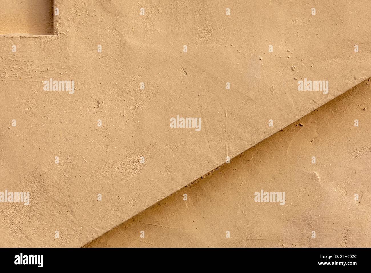 Horizontal close-up image of a beige stucco wall, a small indentation ...