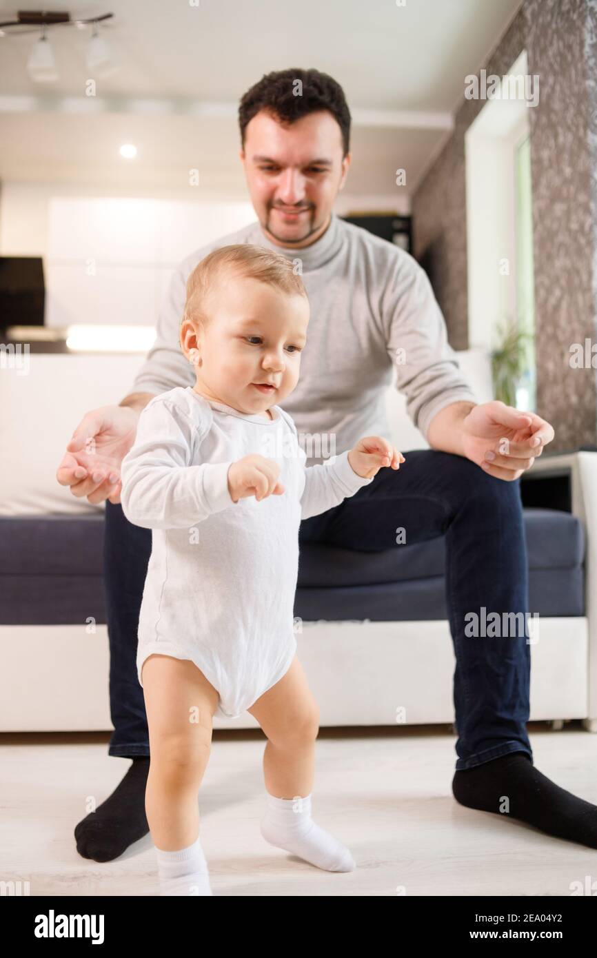 First child steps with fathers support. Infant baby tries to walk on ...