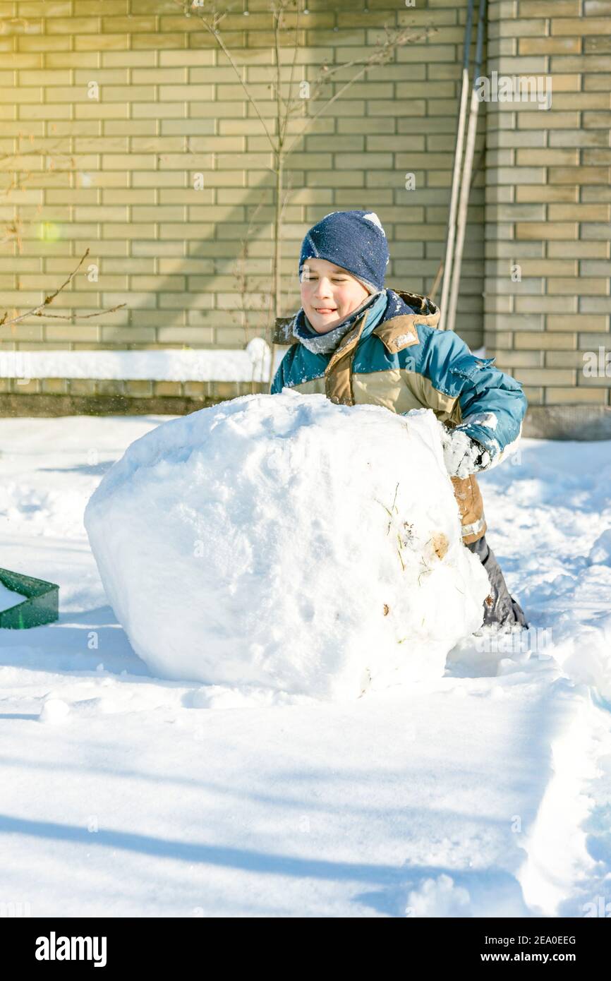 boy sculpt a snowman in the backyard of the house clear winter day. The ...