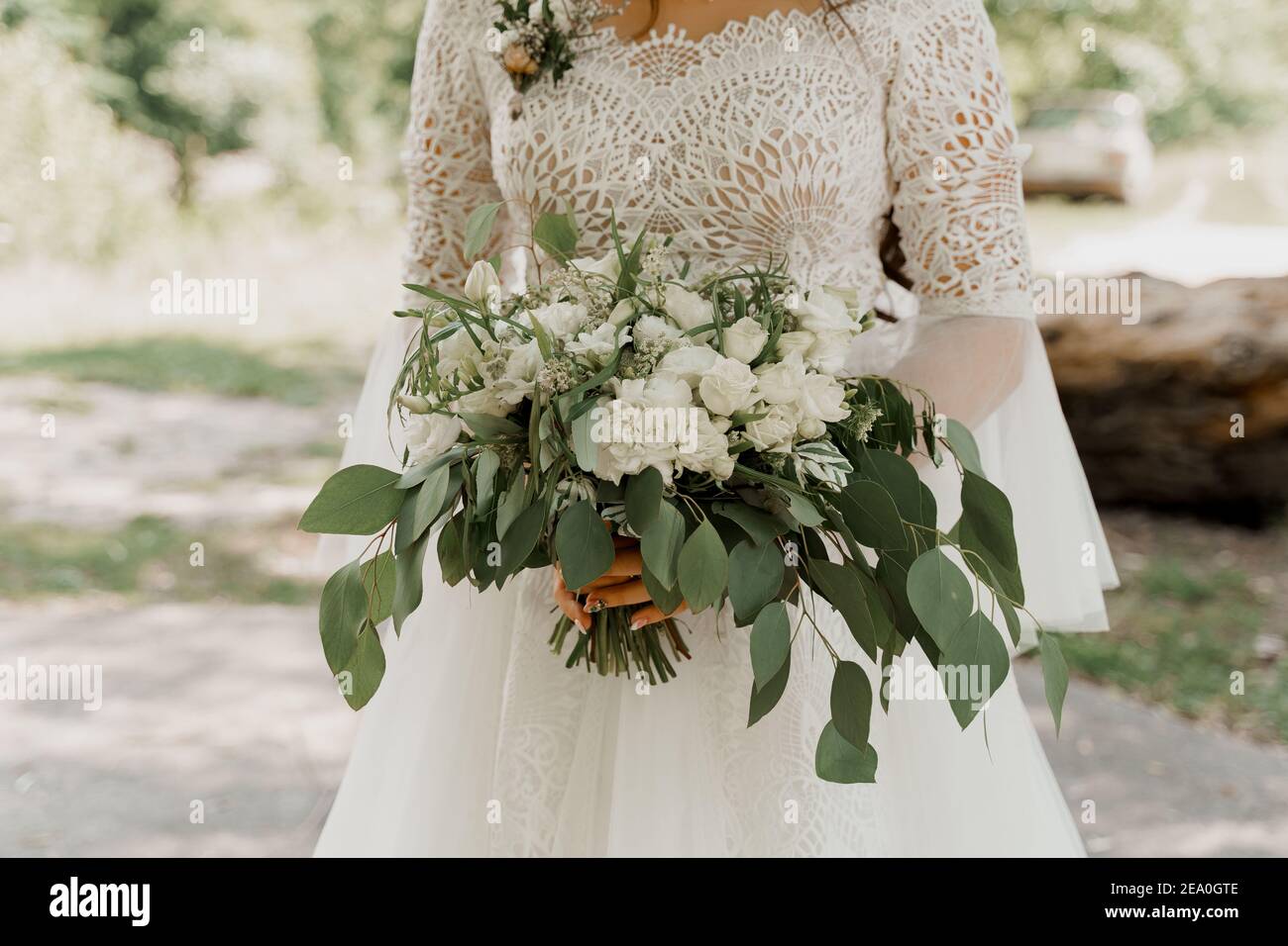 Wedding bouquet with white roses and green leaves. Bride in dress holds ...