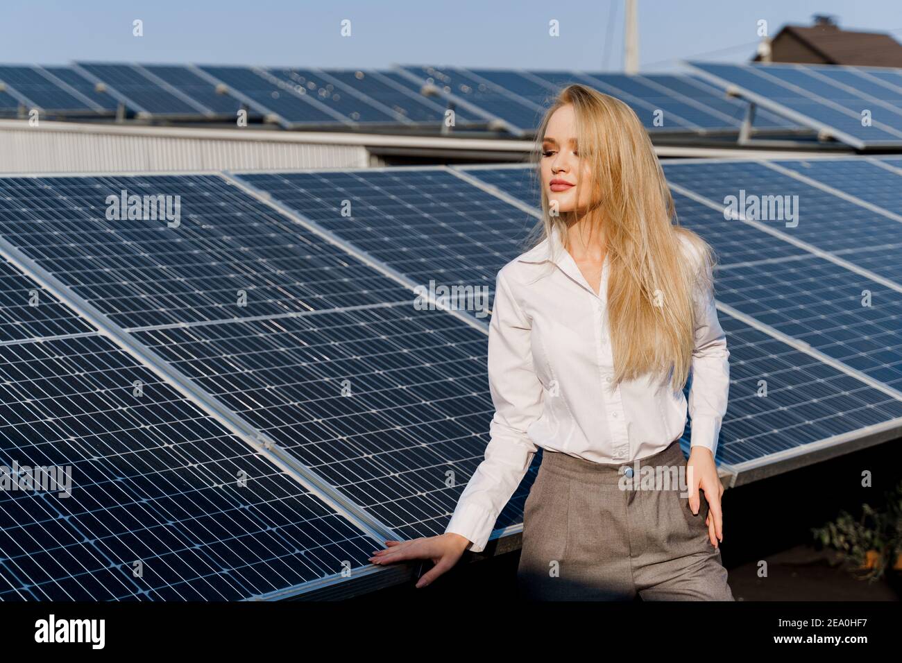 Woman leans on solar panels. Blonde dressed white formal shirt on the ...
