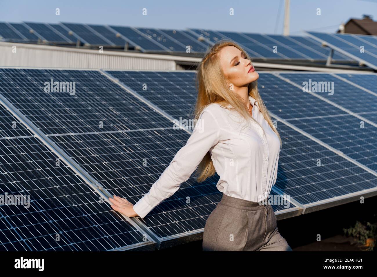 Woman leans on solar panels. Blonde dressed white formal shirt on the ...