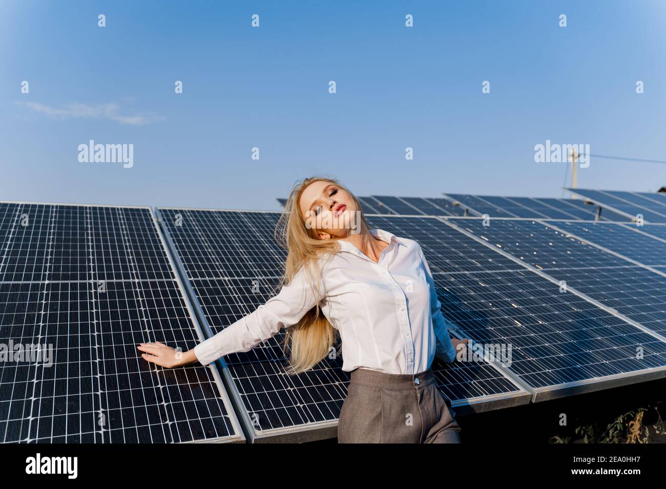 Woman leans on solar panels. Blonde dressed white formal shirt on the ...