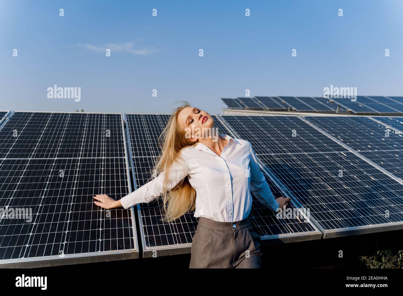 Woman leans on solar panels. Blonde dressed white formal shirt on the ...