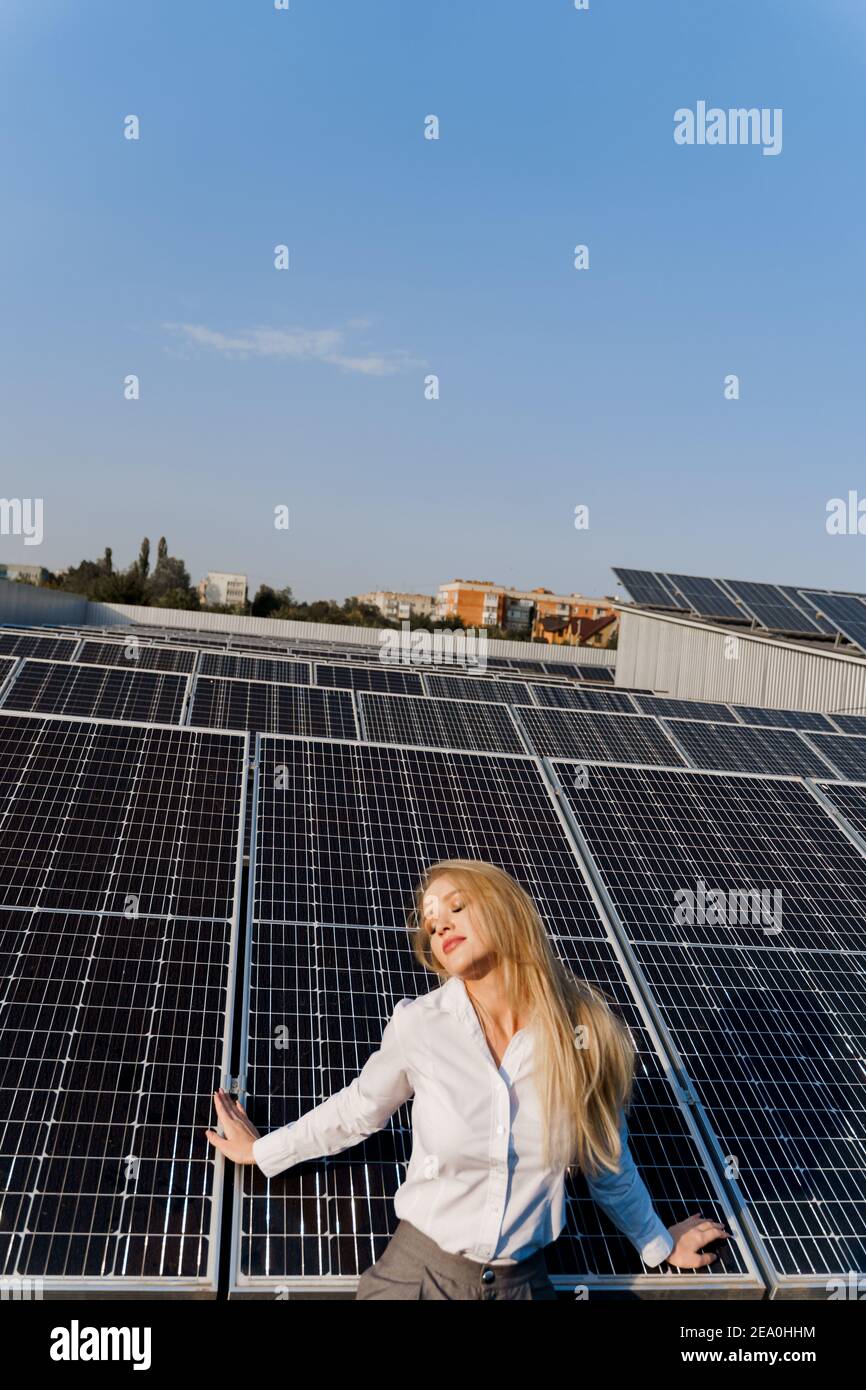 Woman leans on solar panels. Blonde dressed white formal shirt on the ...