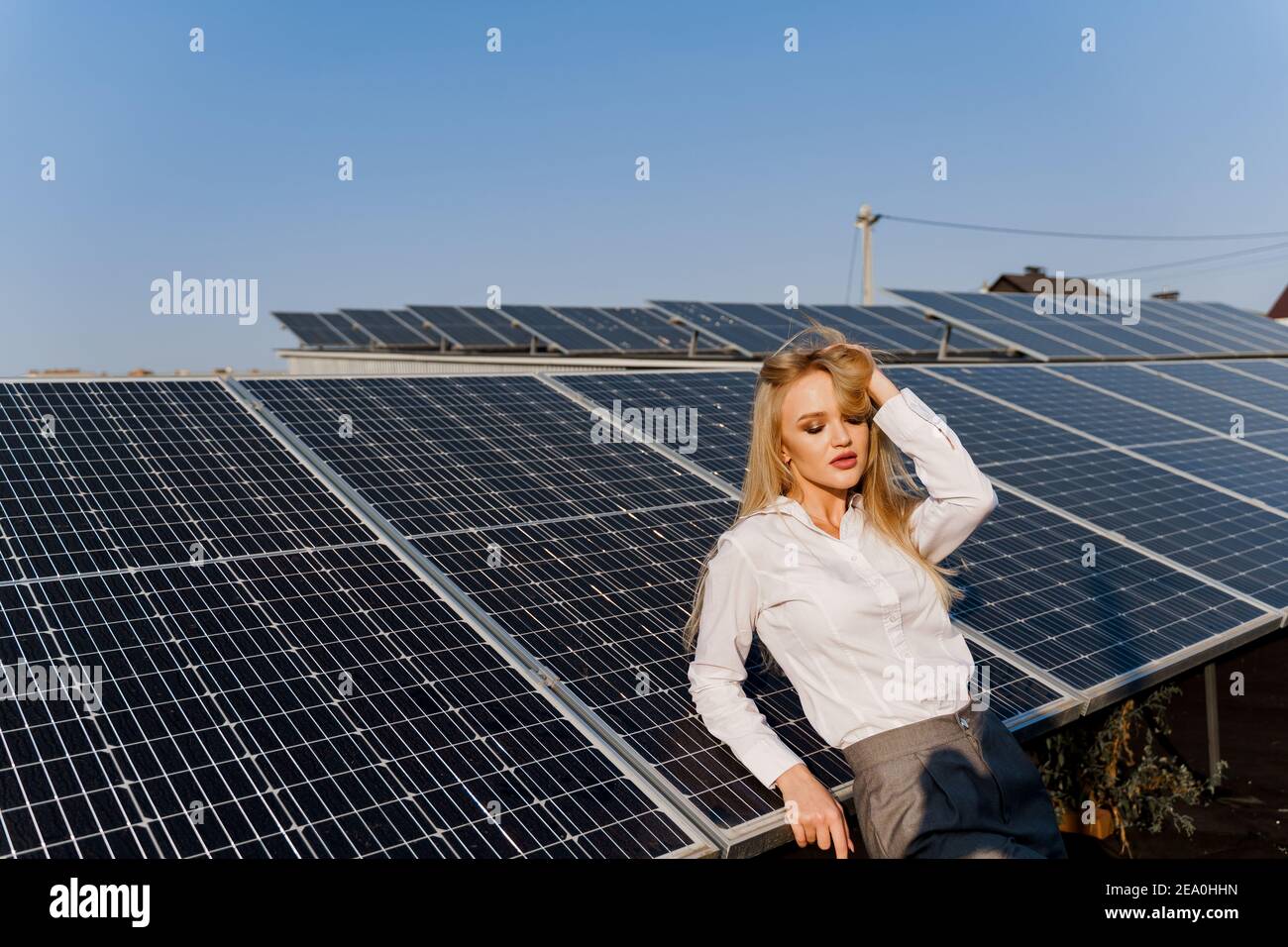 Woman leans on solar panels. Blonde dressed white formal shirt on the ...