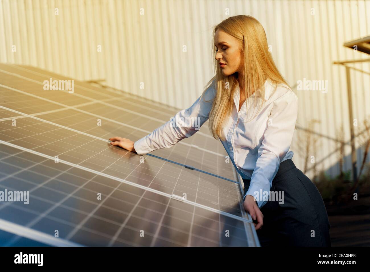 Woman leans on solar panels. Blonde dressed white formal shirt on the ...