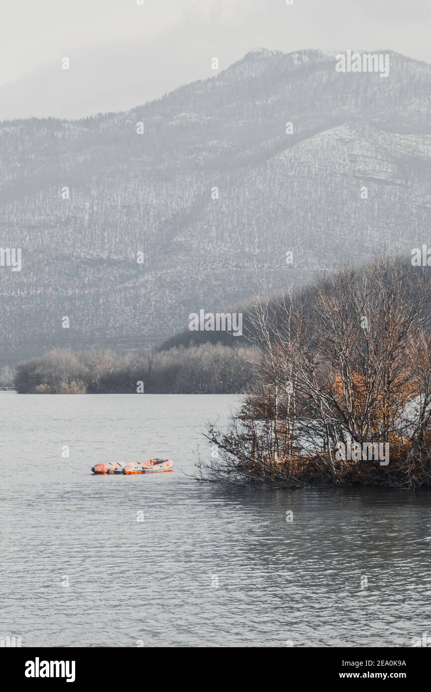 Vertical shot of a kayak on the river on the background of a snowy mo ...