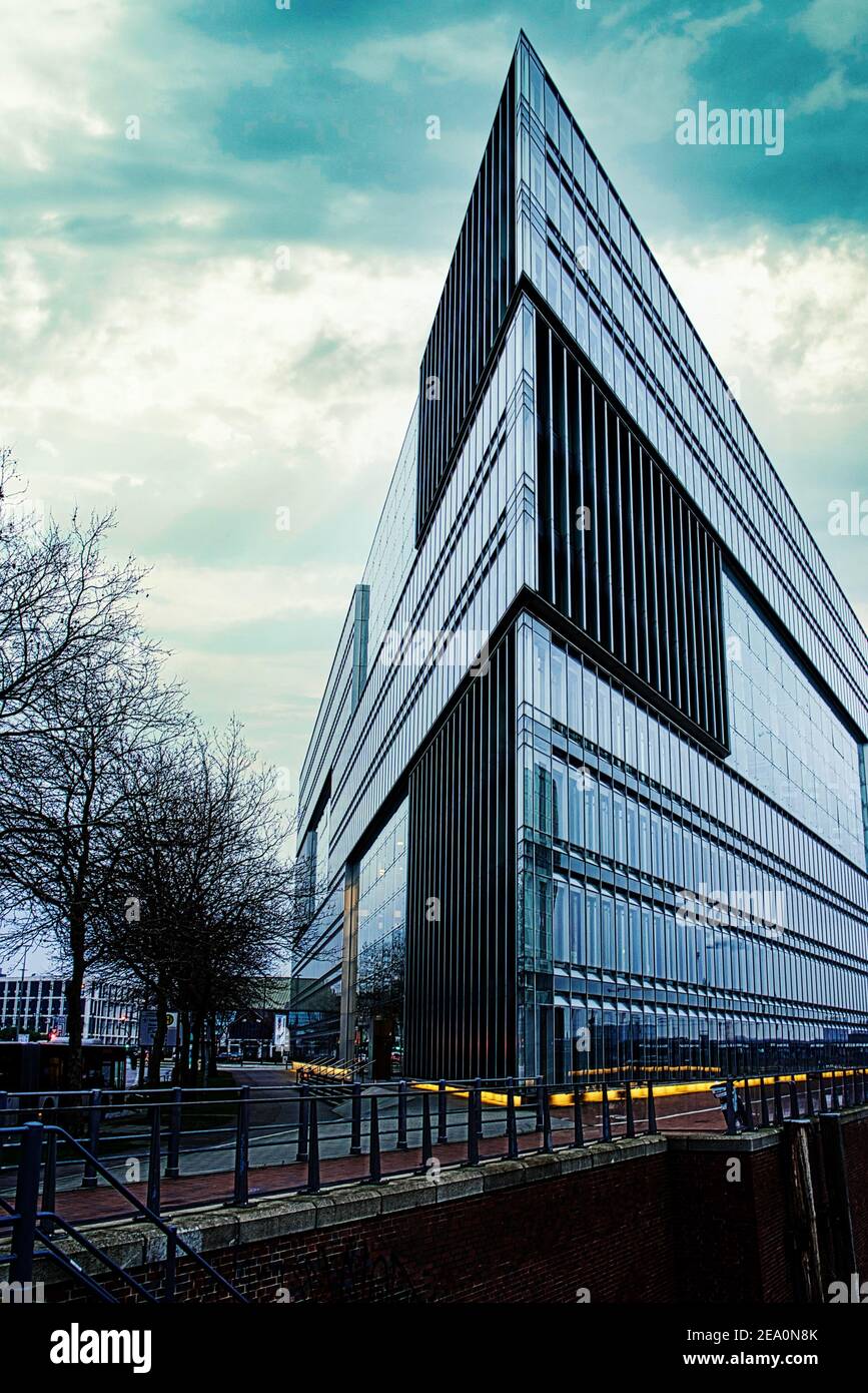 A vertical shot of a modern triangle building with glass in the cloudy ...