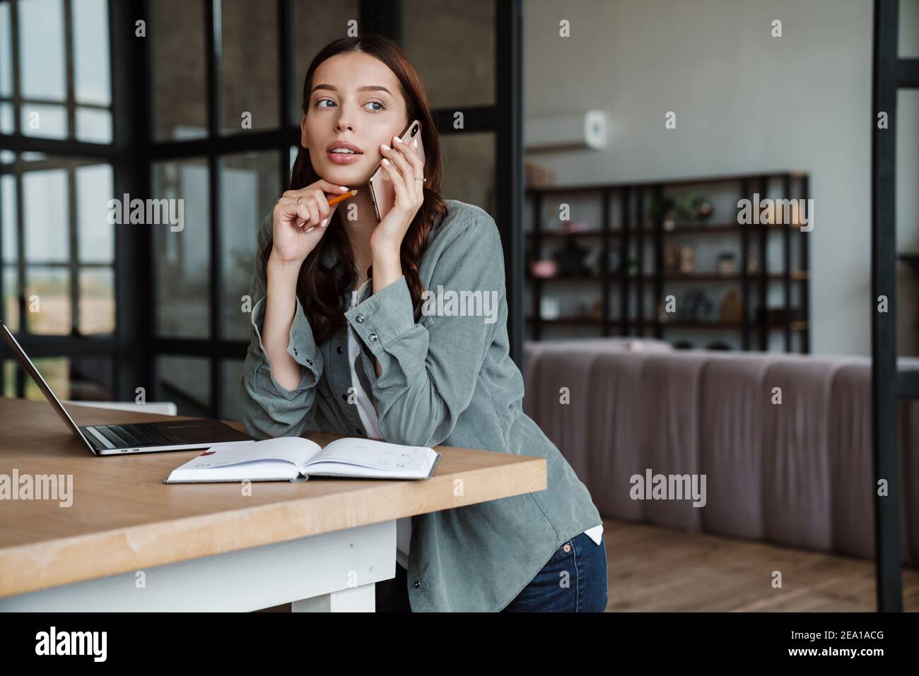 Beautiful serious woman talking on cellphone while working with laptop ...